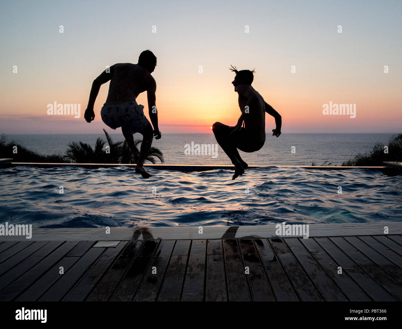 Two boys jump into an infinity pool at sunset Stock Photo - Alamy