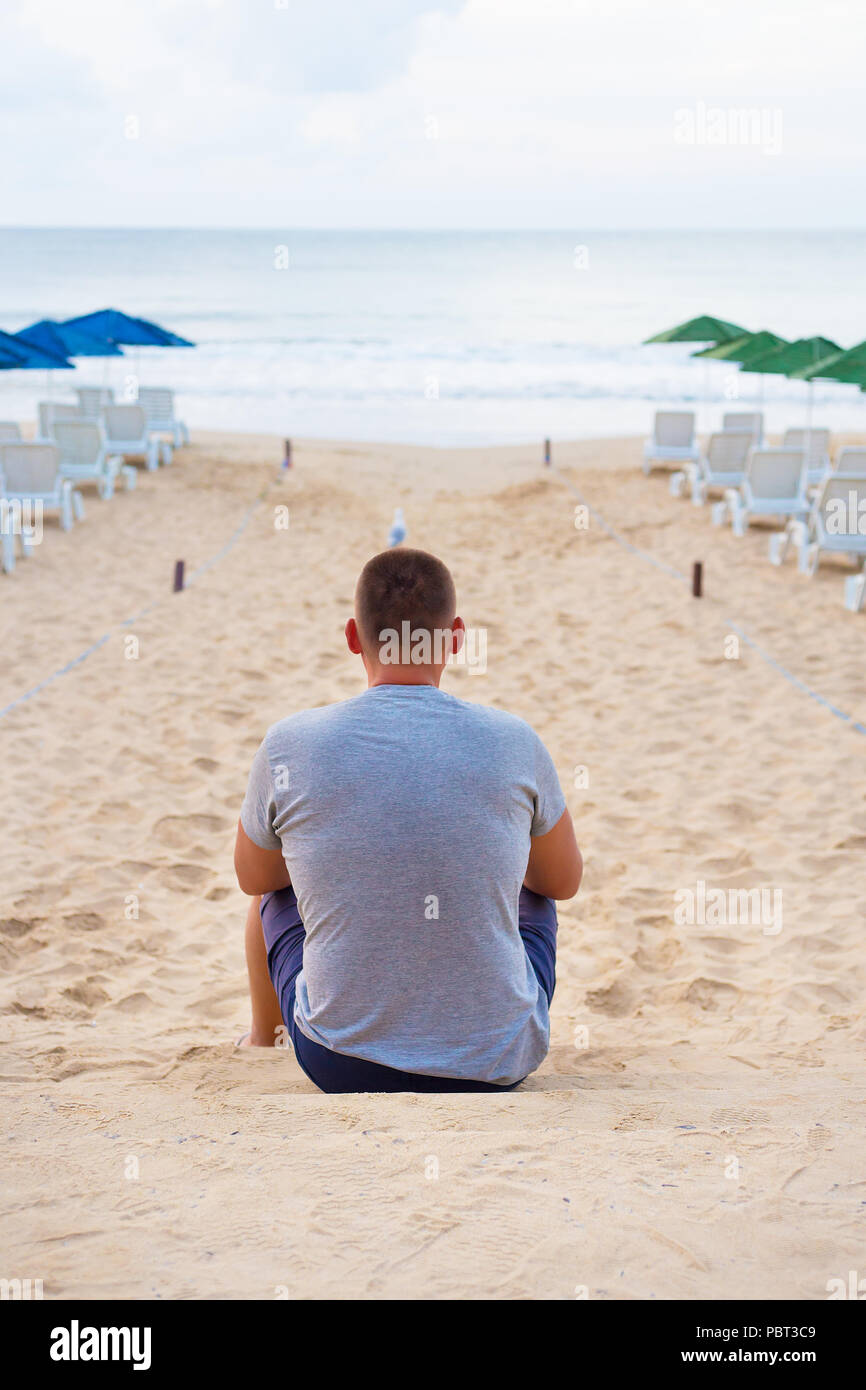 Young guy sits with his back on a sandy beach Stock Photo - Alamy