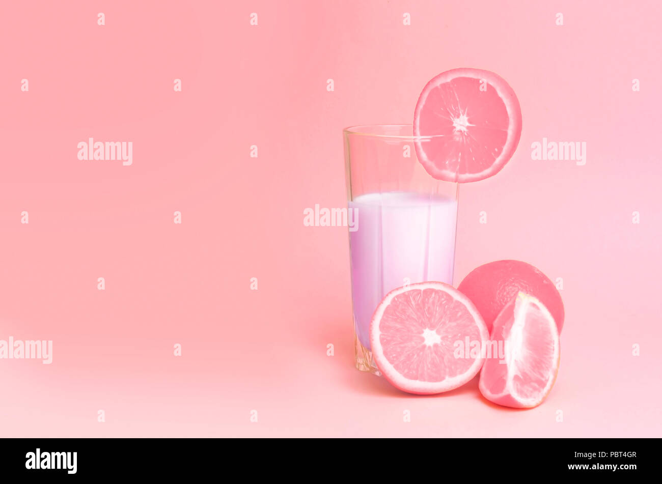 A glass with pink orange juice with the cut oranges on a pink ...
