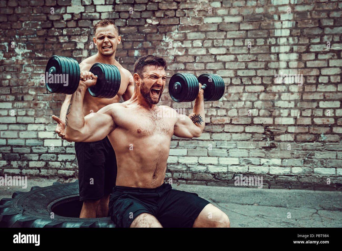 Two muscular athletes training, one raise, push the dumbbell when other ...
