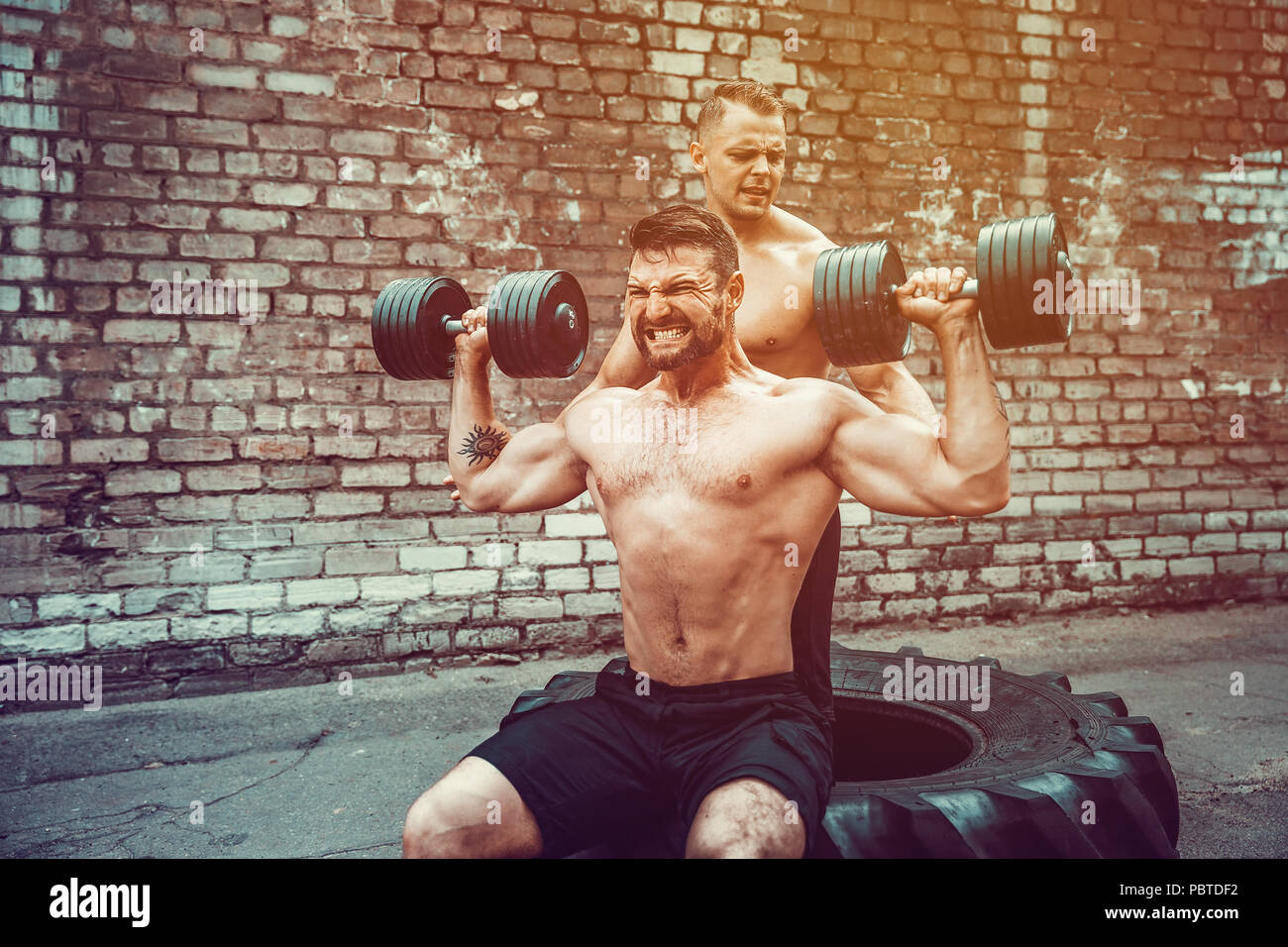 Two muscular athletes training, one raise, push the dumbbell when other ...