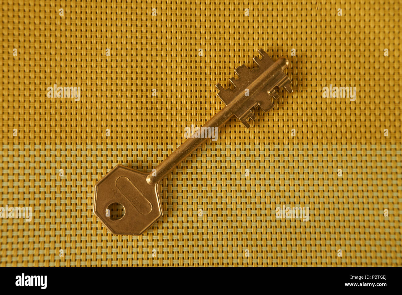 Golden key on two toned woven yellow textile. Conceptual key as symbol ...