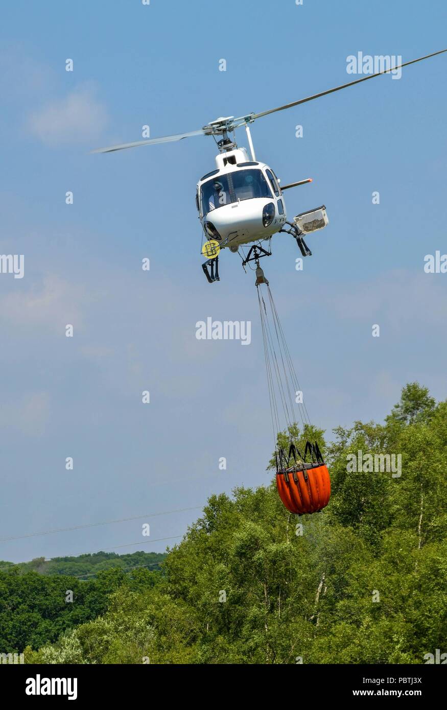 A helicopter carrying a large bucket of water. The helicopter is being ...