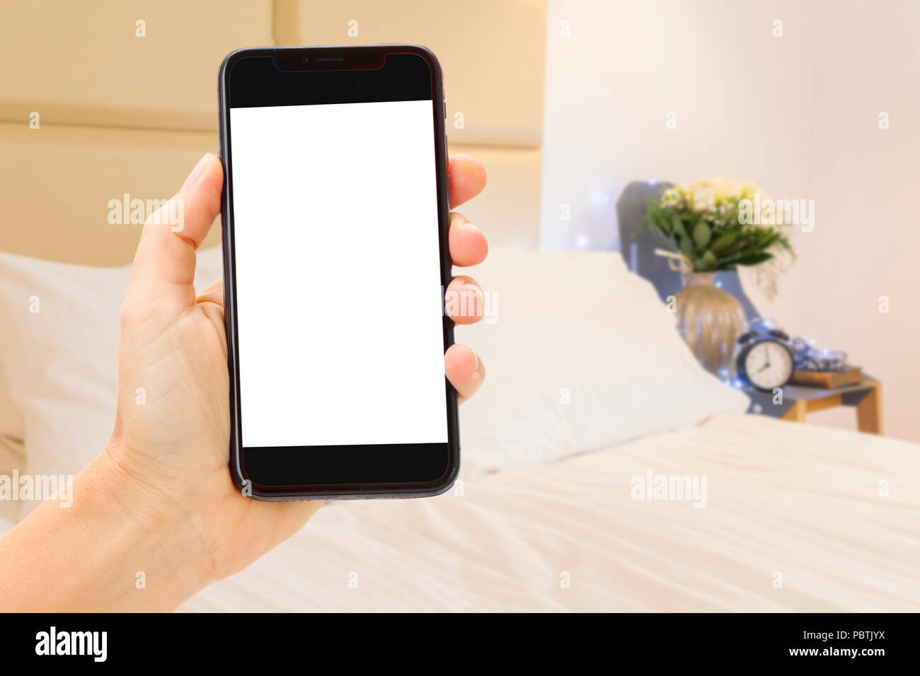 hand holding phone with empty screen on bed with white linen and ...
