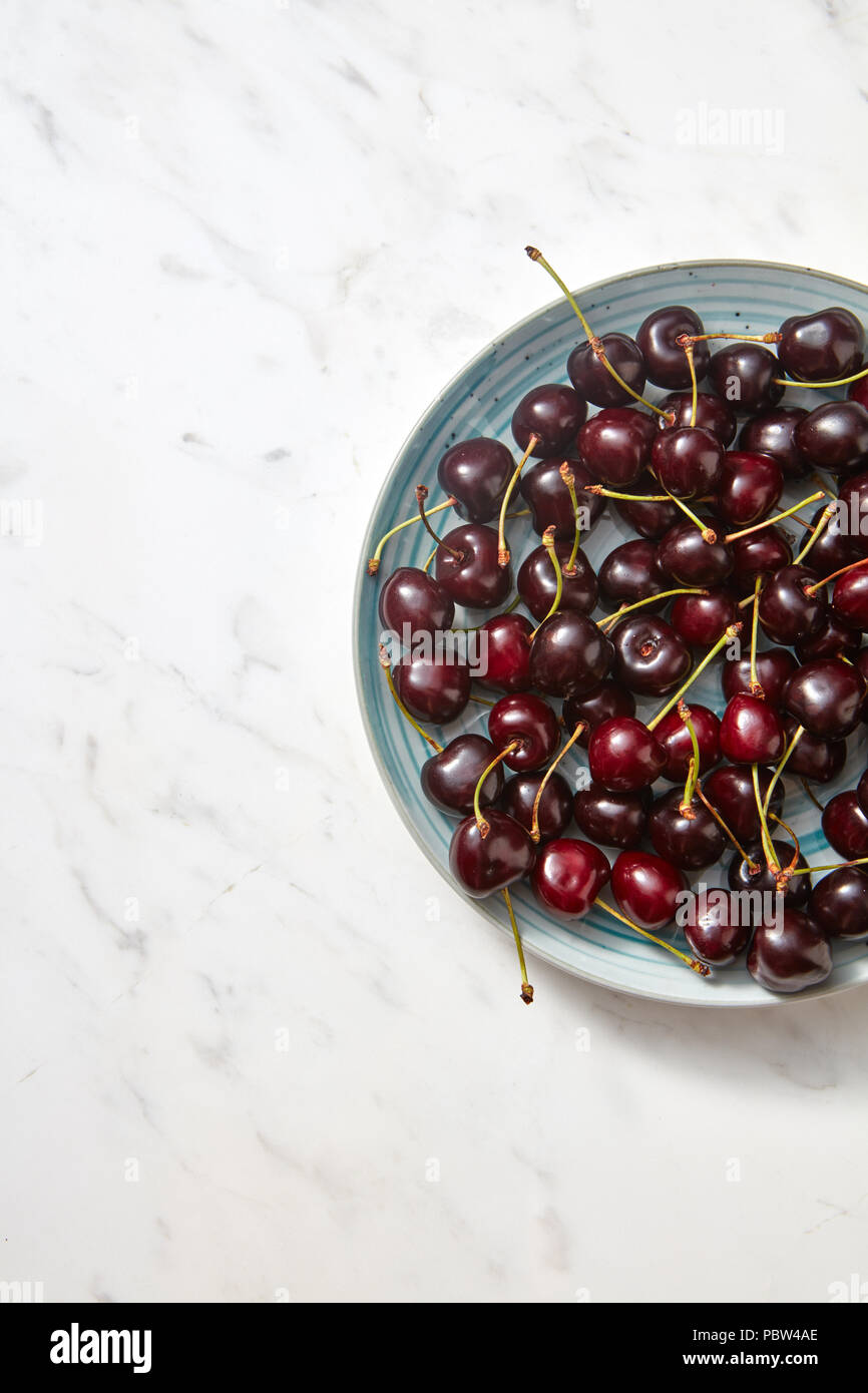 A pile of ripe sweet dark red cherries in a blue ceramic plate on a ...