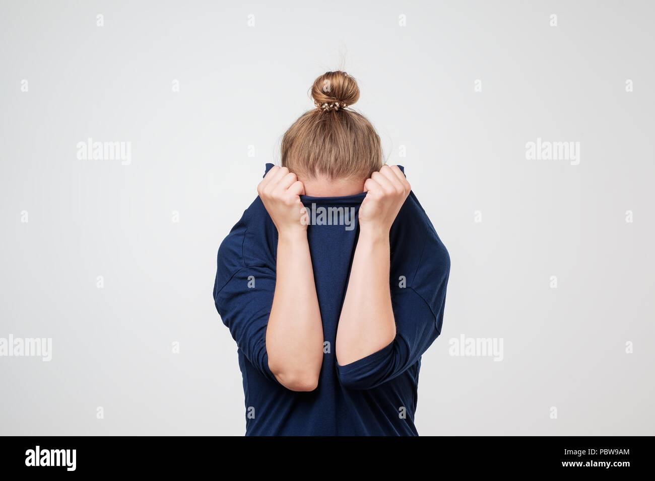 European woman hiding face under the clothes. She is oulling sweater on ...