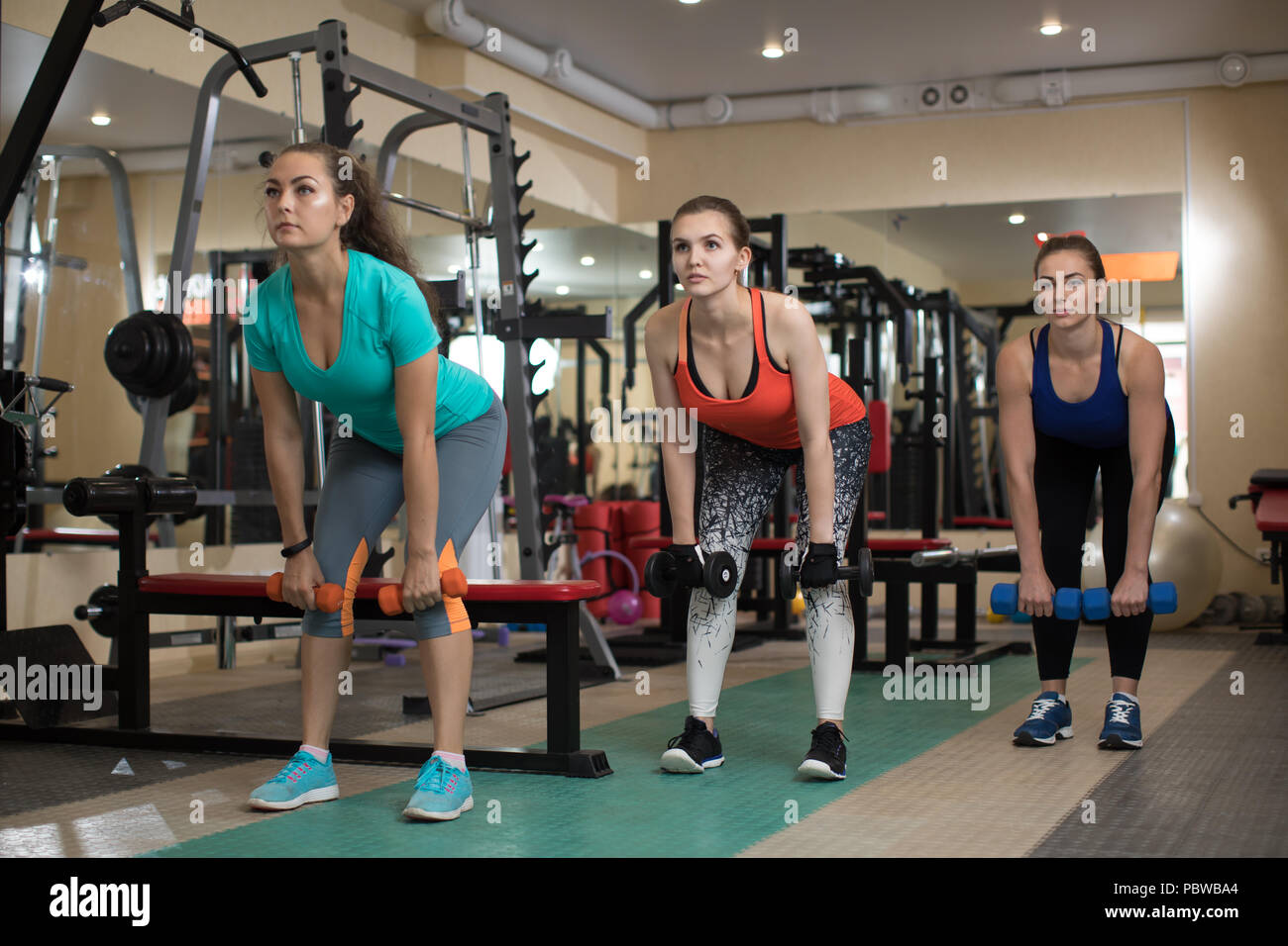 Three pretty fitness active girls doing exercises with kettlebells in ...