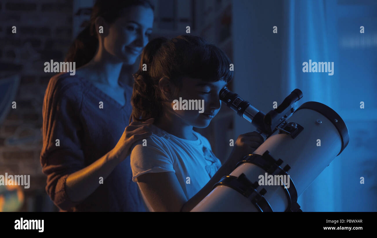 Cute sisters watching the stars together at home using a telescope ...