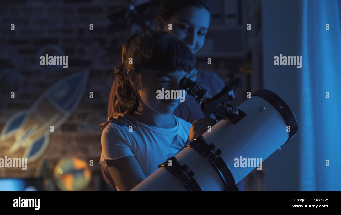 Cute sisters watching the stars together at home using a telescope ...