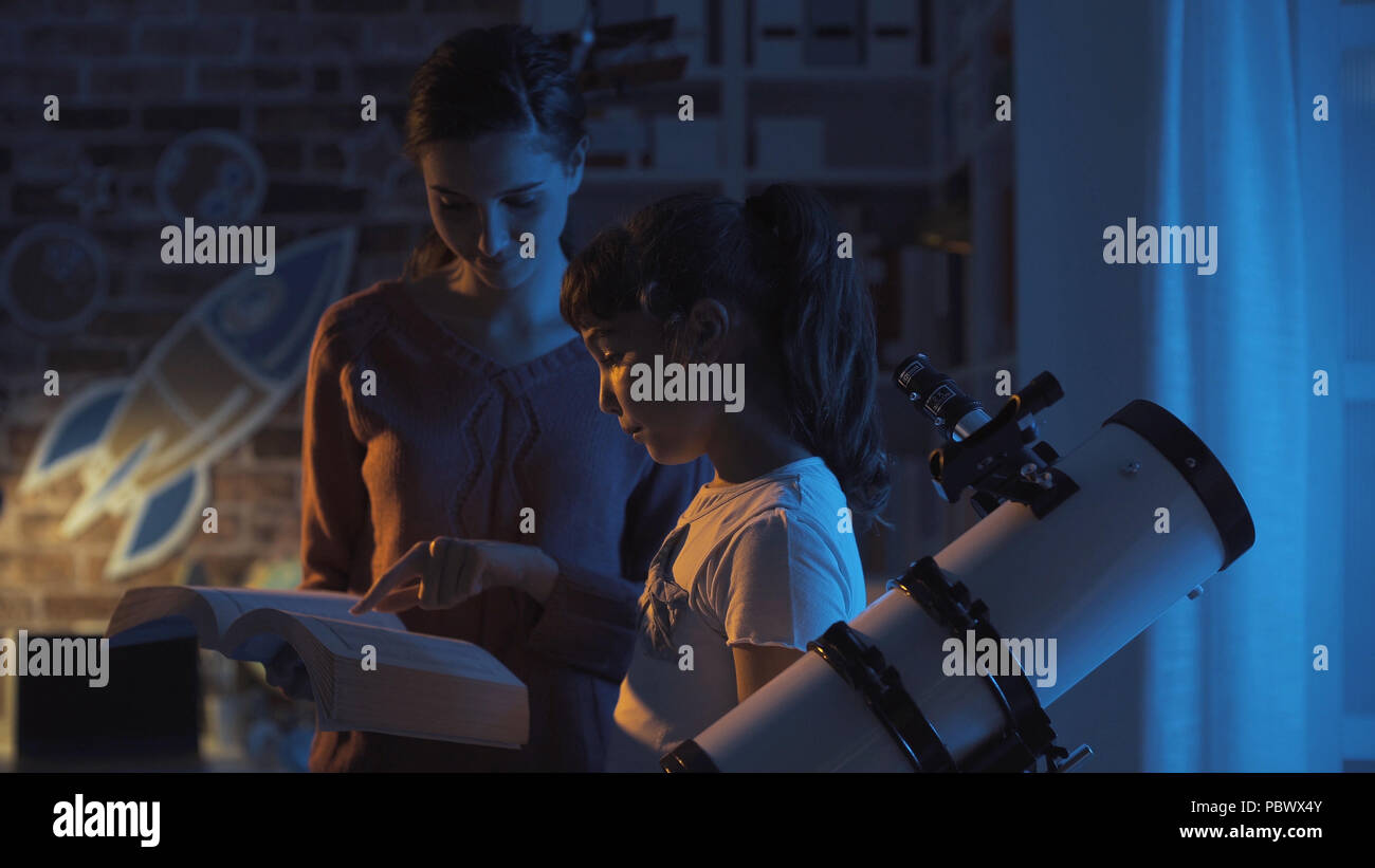 Young girls at home studying astronomy on a book and watching the stars ...