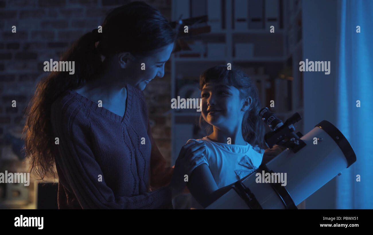Cute sisters watching the stars together at home using a telescope ...