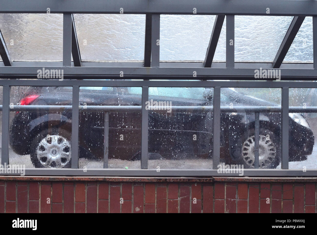 Strong rain on a window with wooden frames, behind the window is a car ...