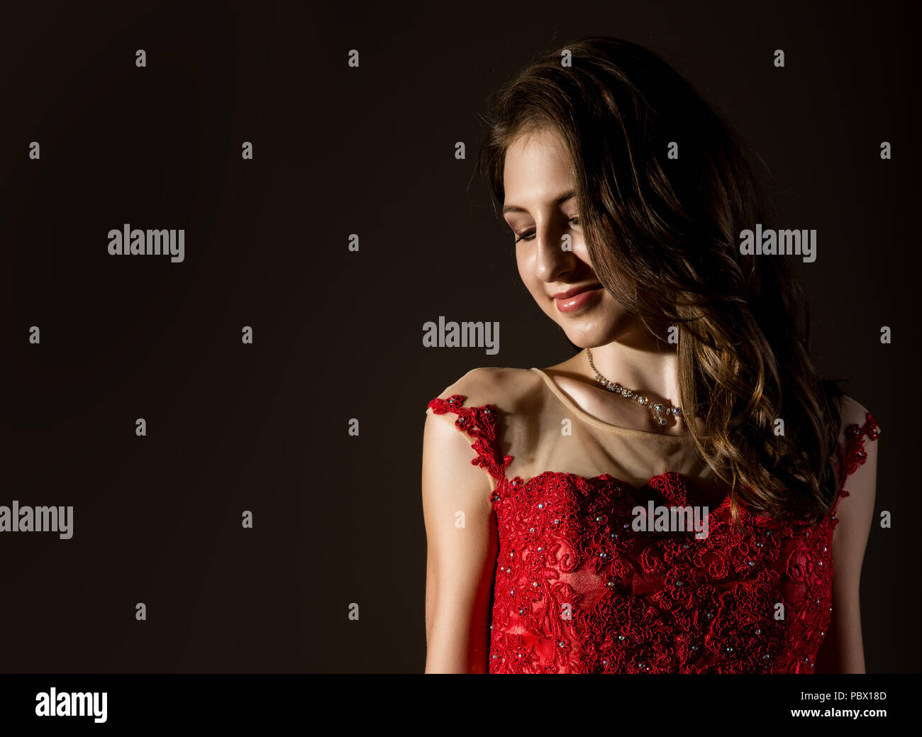 Shy woman lowered her eyes smiles timid. Girl in elegant red dress on a ...