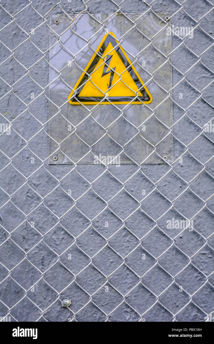 Danger of electrocution yellow sign on gray background with metal wire ...