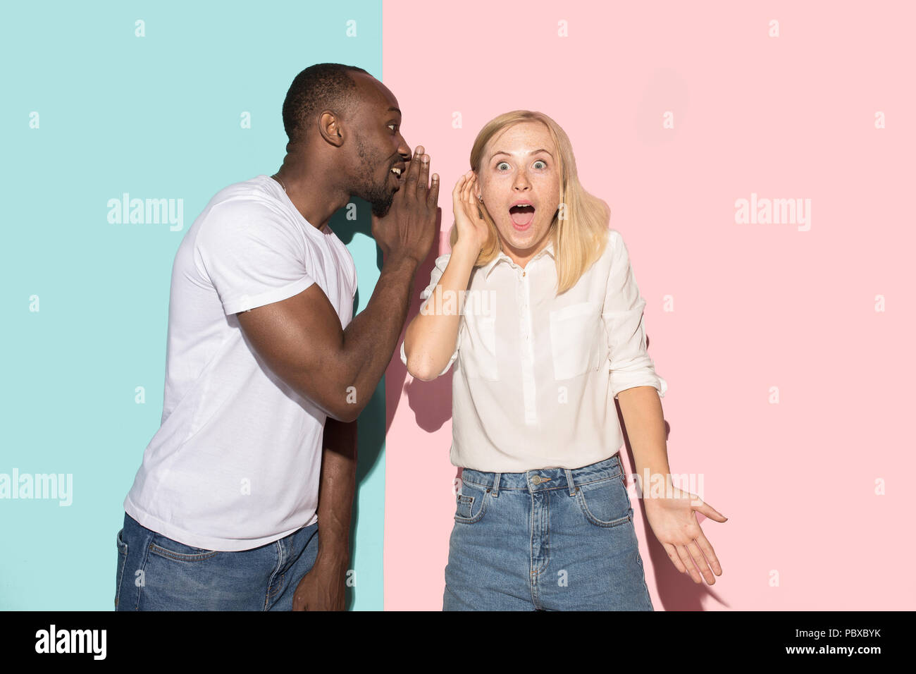 The young couple whispering a secret behind her hand over studio ...