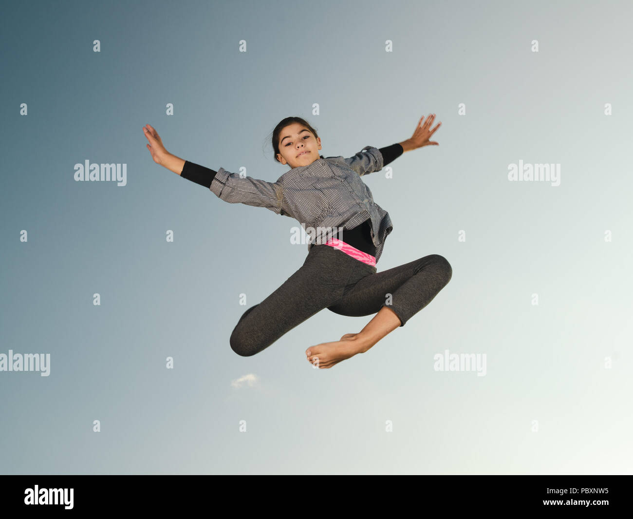 Smiling, happy young girl gymnast acrobat jumping high in the sky Stock ...