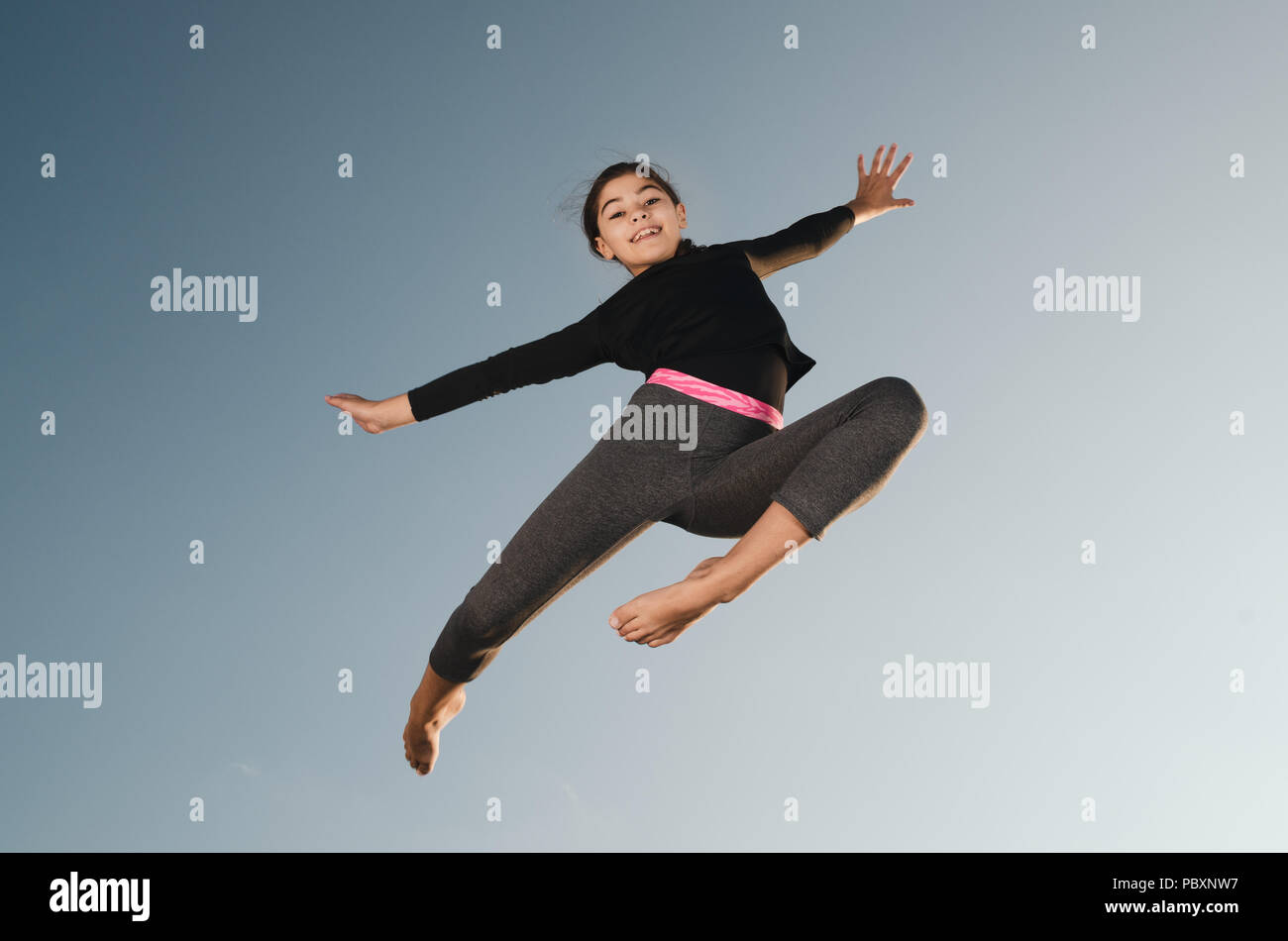 Smiling, happy young girl gymnast acrobat jumping high in the sky Stock ...