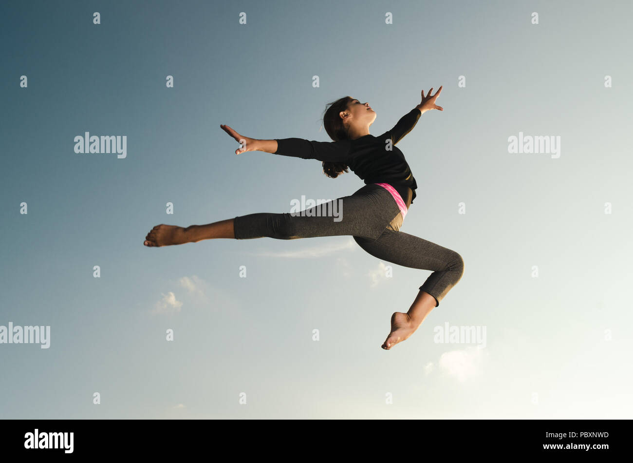 Smiling, happy young girl gymnast acrobat jumping high in the sky Stock ...