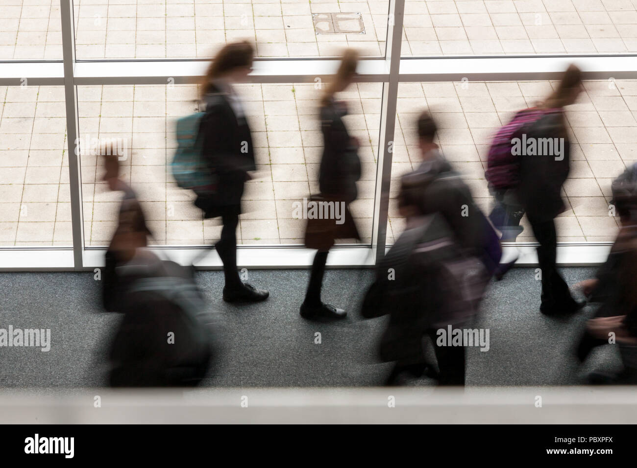 Secondary school pupils moving by a window in a school UK, blurred ...