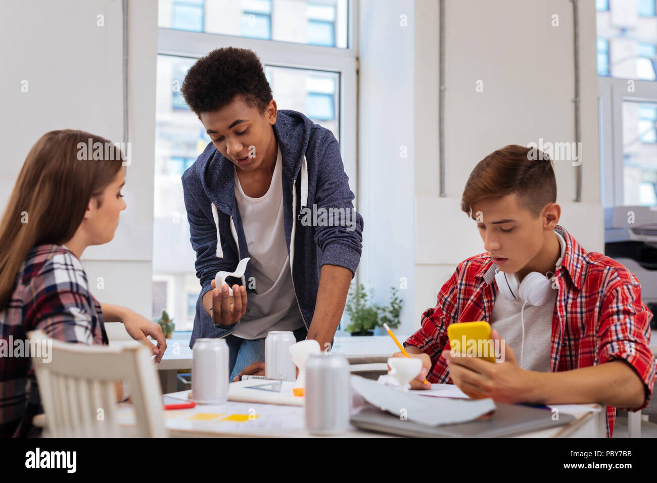 Dark-haired student wearing grey sport jacket holding model of chair ...