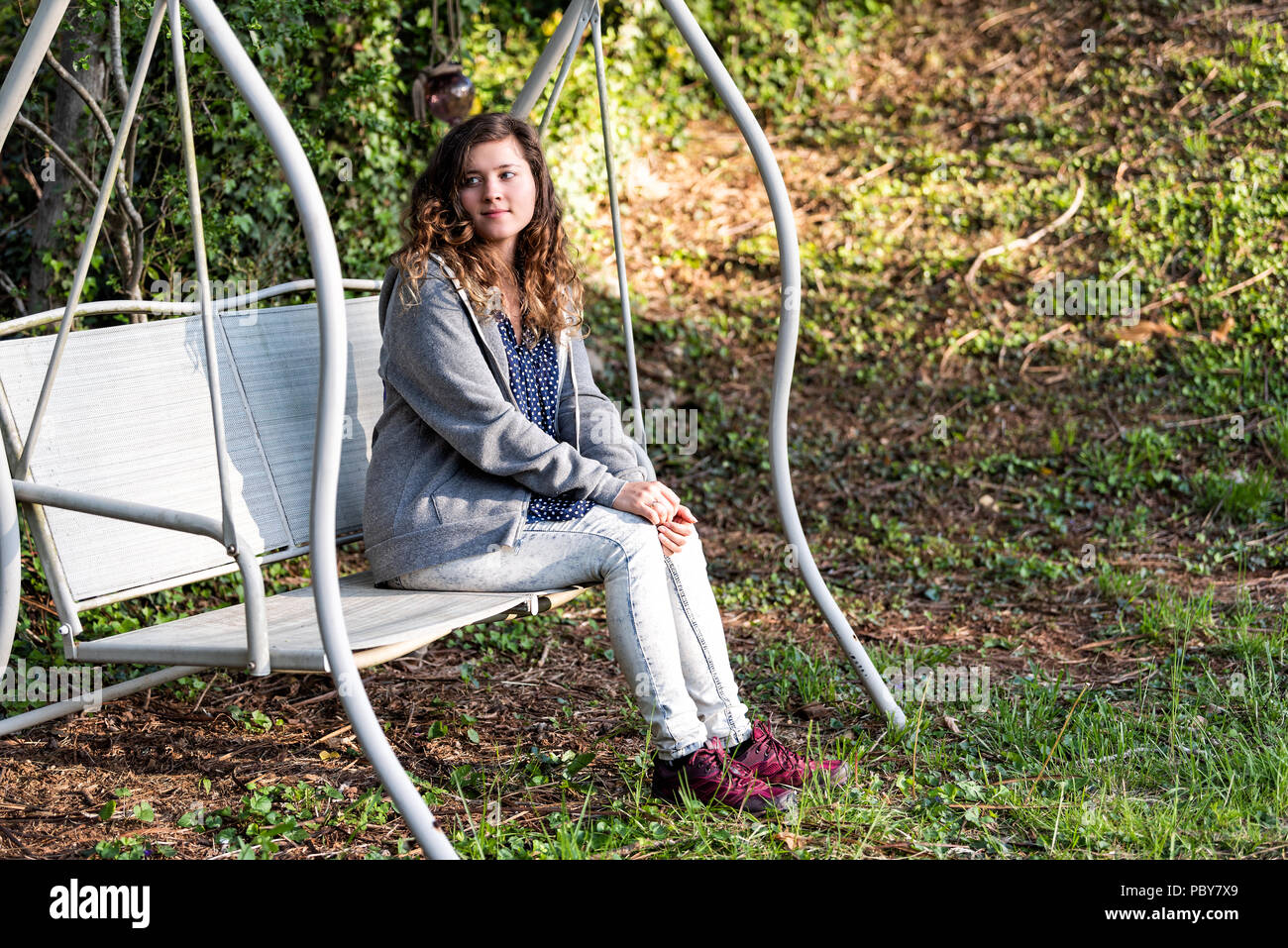 Young woman sitting on garden swing in morning, happy, enjoying fresh ...