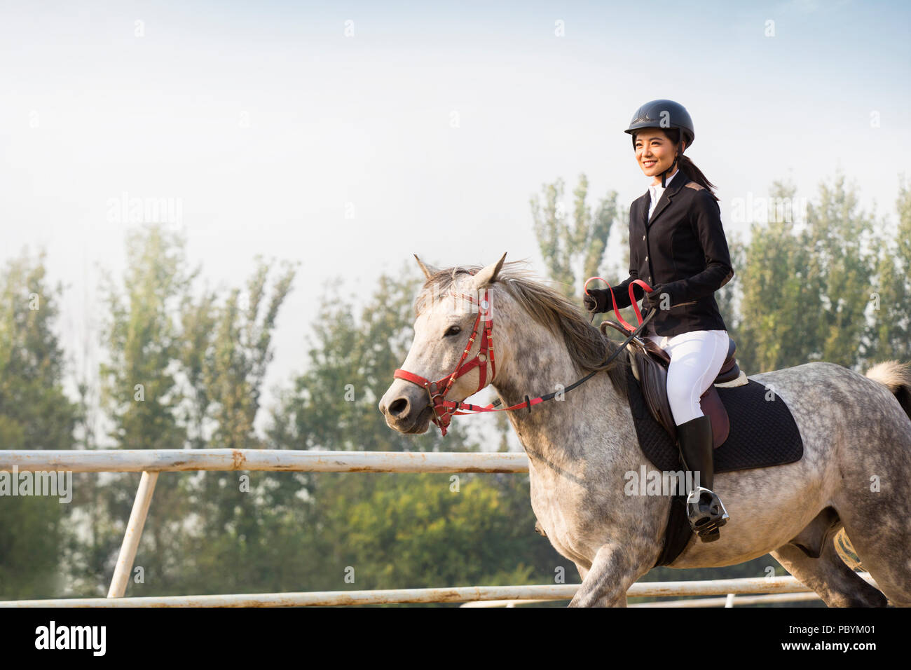 Cheerful young Chinese woman riding horse Stock Photo - Alamy