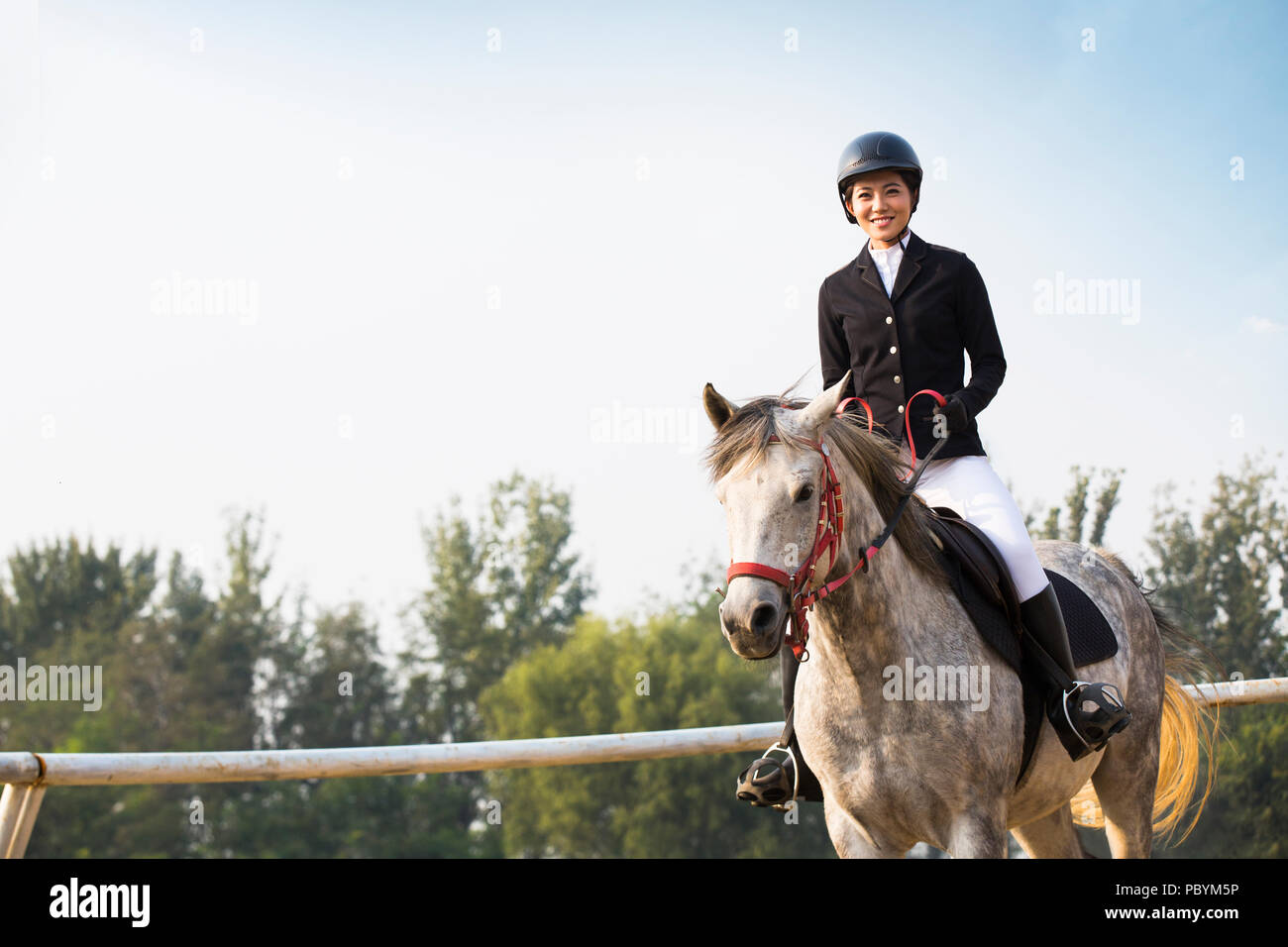 Cheerful young Chinese woman riding horse Stock Photo - Alamy
