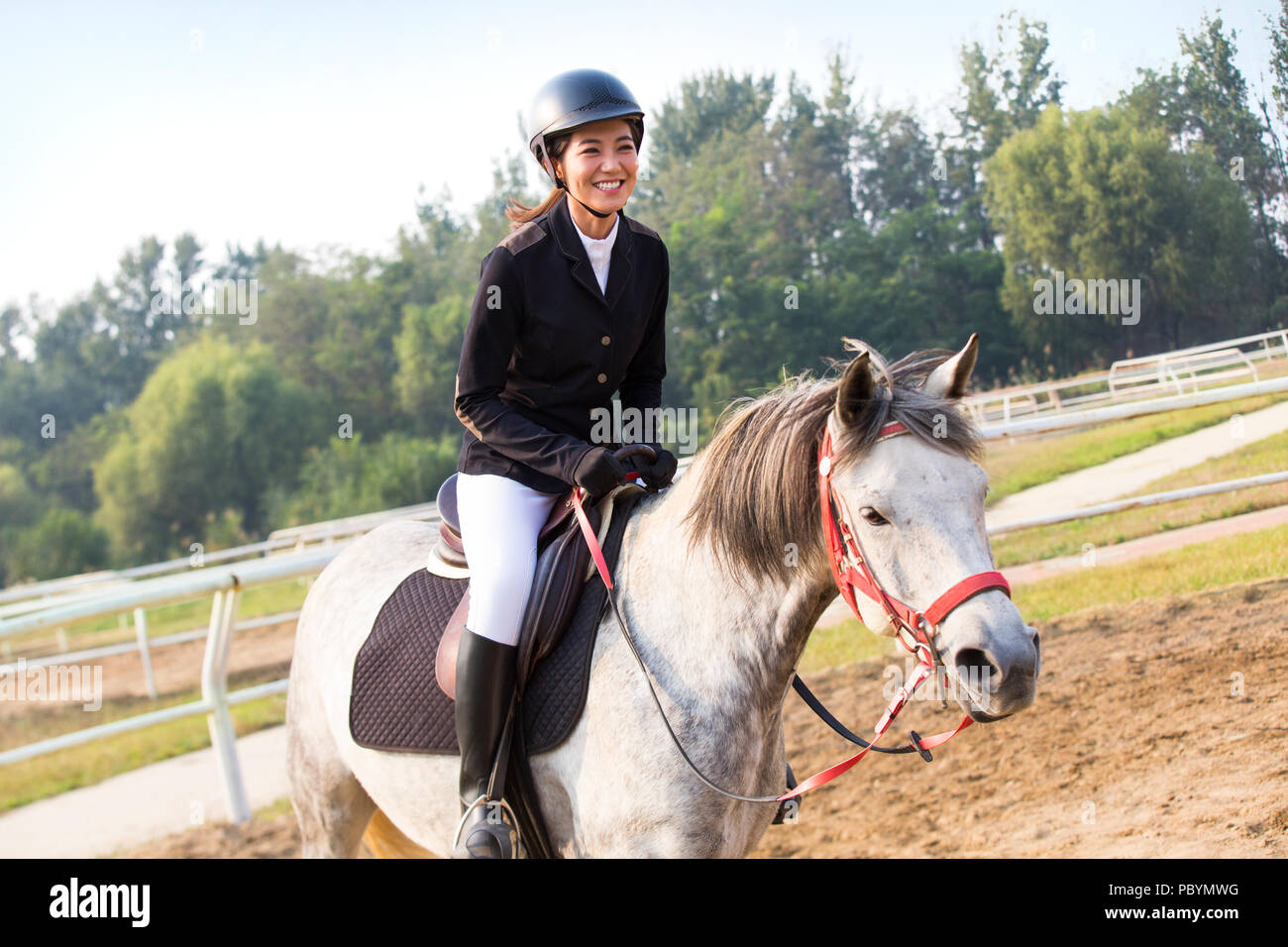 Cheerful young Chinese woman riding horse Stock Photo - Alamy