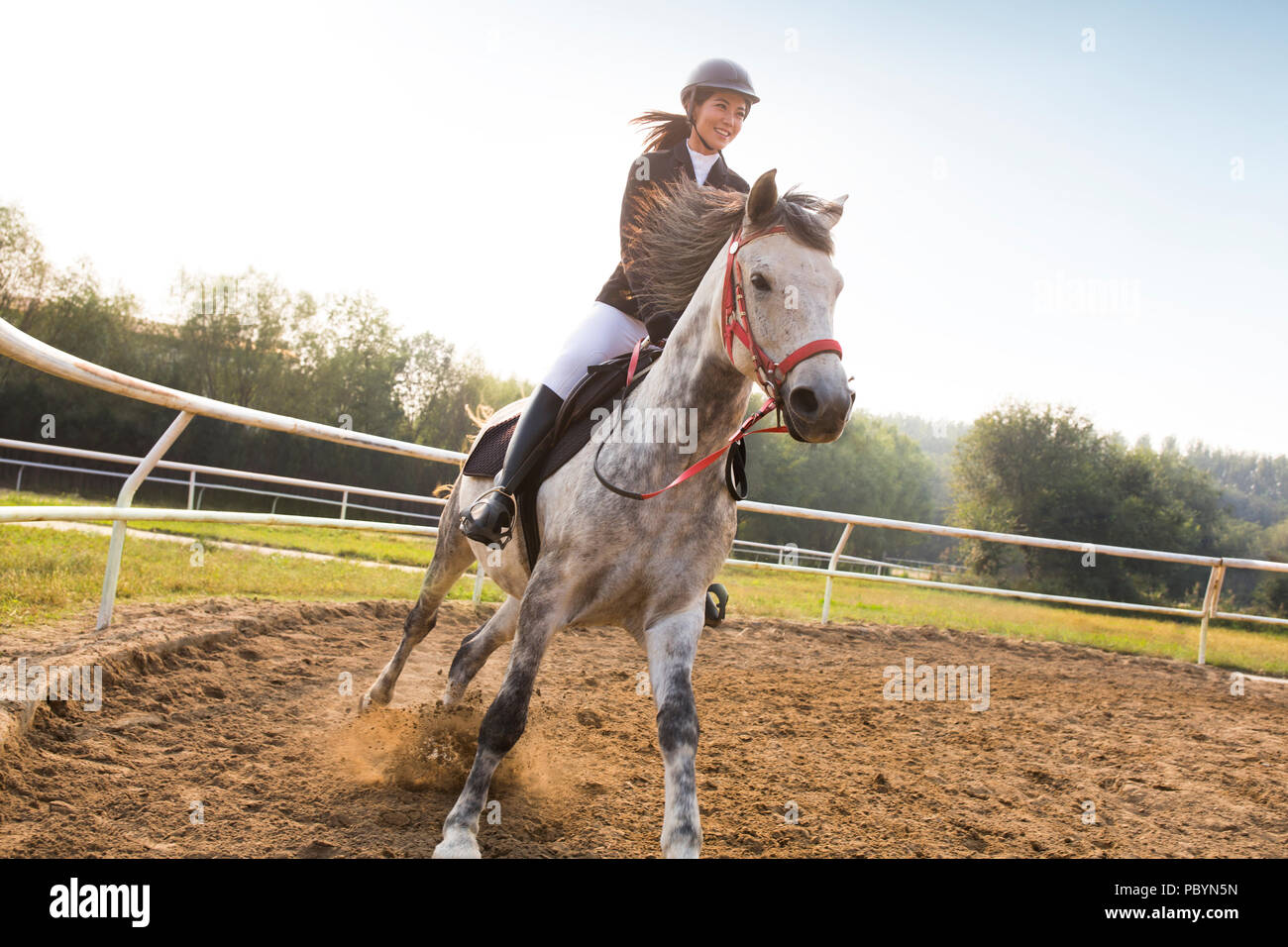 Cheerful young Chinese woman riding horse Stock Photo - Alamy