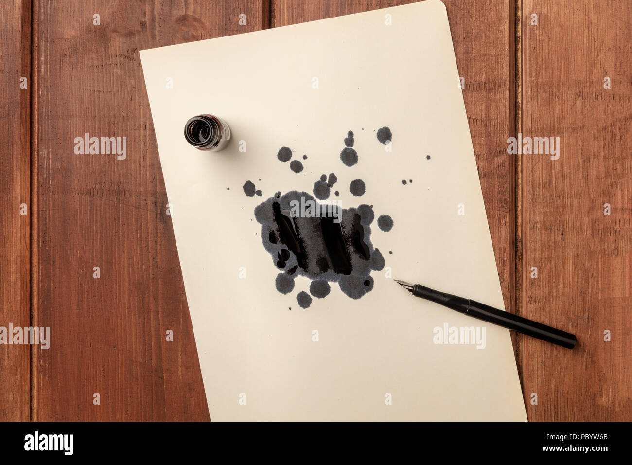An overhead photo of an ink well with drops of ink and a nib pen, with ...