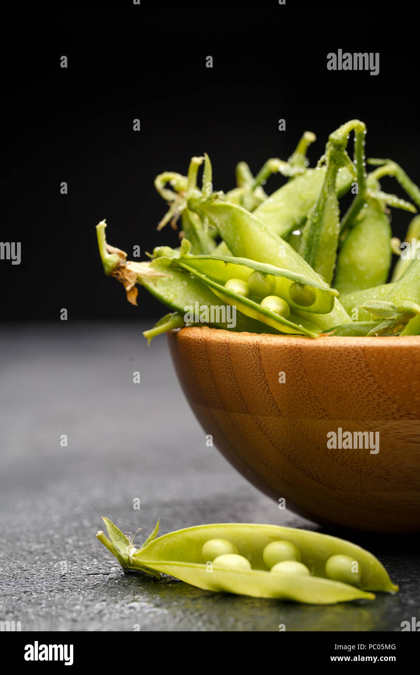 Photo of green pea pods in wooden plate on empty black table with pod ...