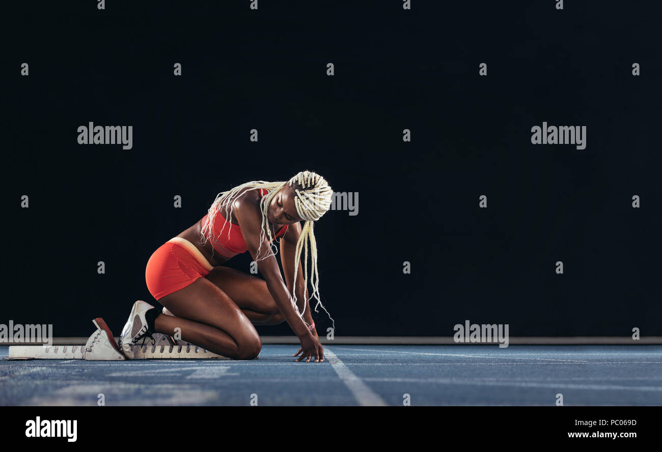 Female athlete looking back at the starting block while taking position ...