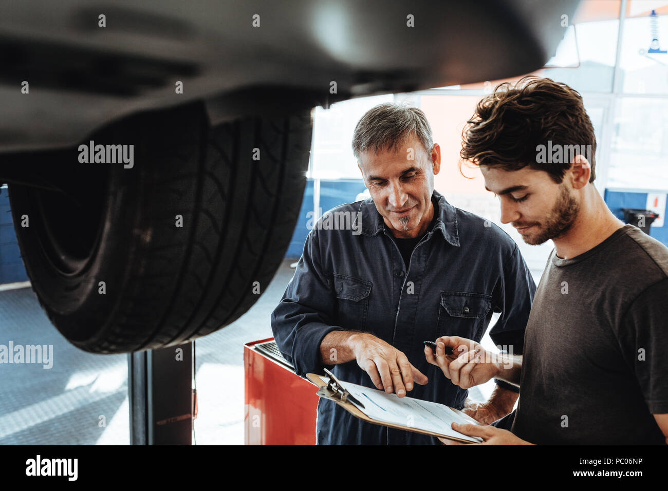 Mechanics in uniform making notes while standing by a car in auto ...