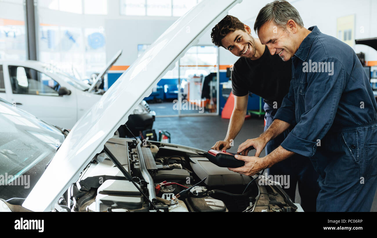 Two happy automobile mechanics doing car engine checkup with a device ...