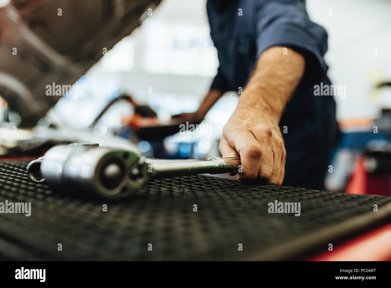 Hand of mechanic picking up a ratchet spanner from table in auto ...