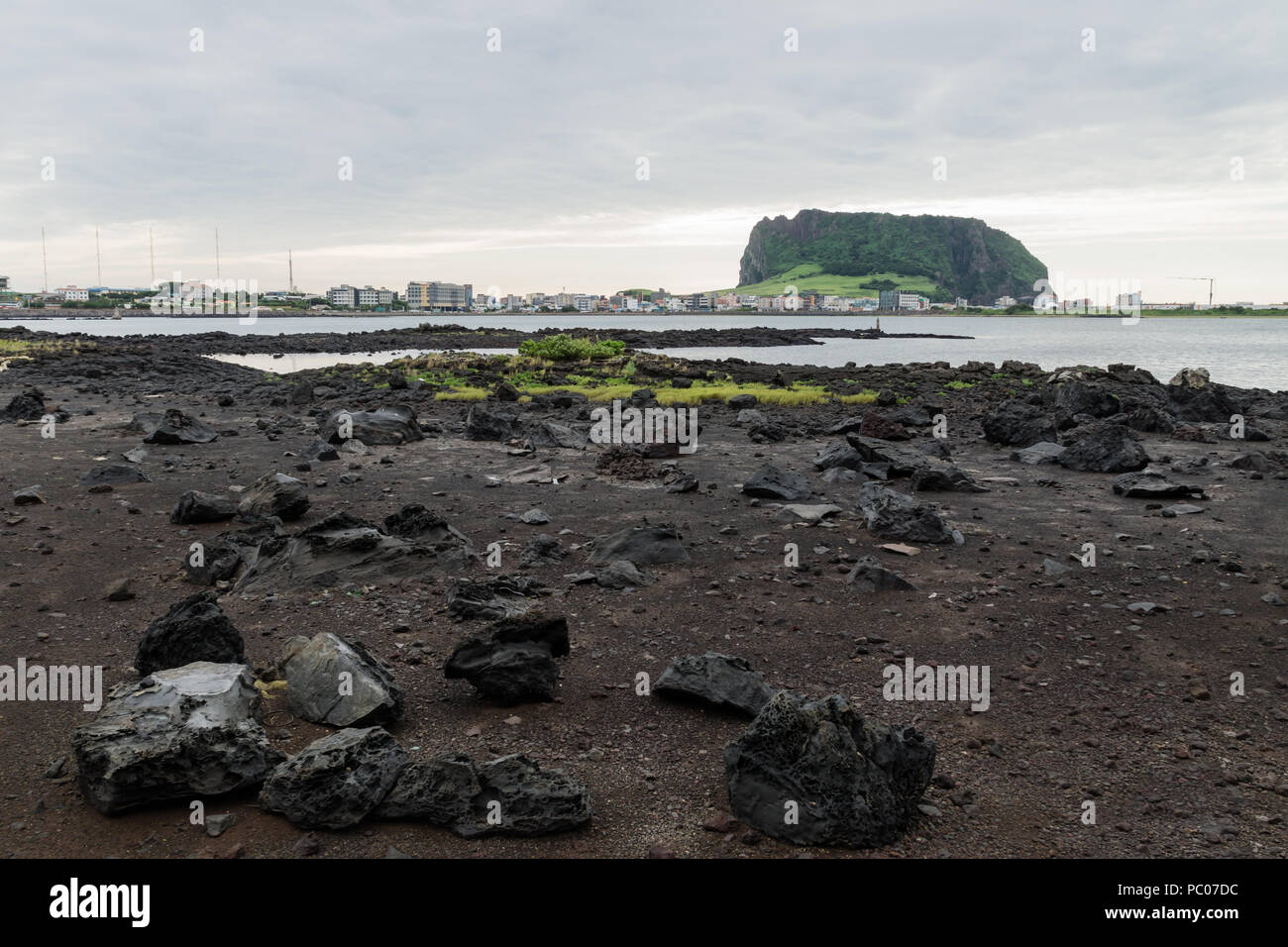 Black lava stones and beach with lake view to green Ilchulbong volcano ...