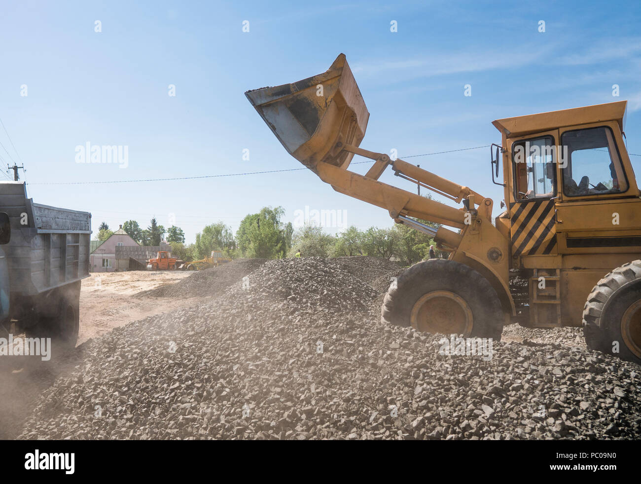 Yellow loader delivering stone gravel into truck during road ...