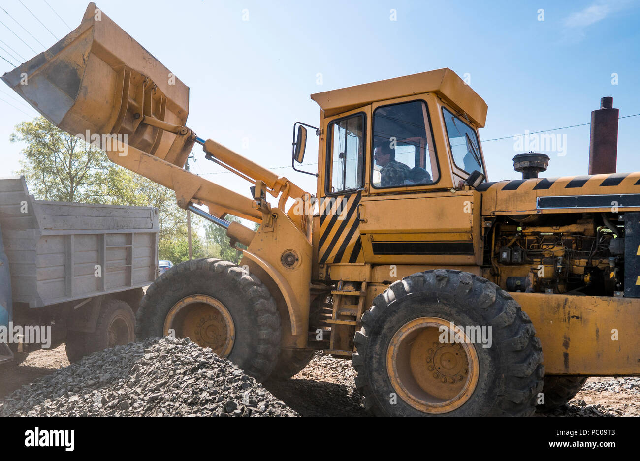 Yellow loader delivering stone gravel into truck during road ...