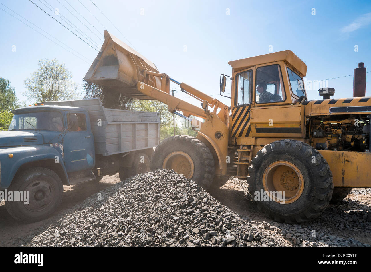 Yellow loader delivering stone gravel into truck during road ...