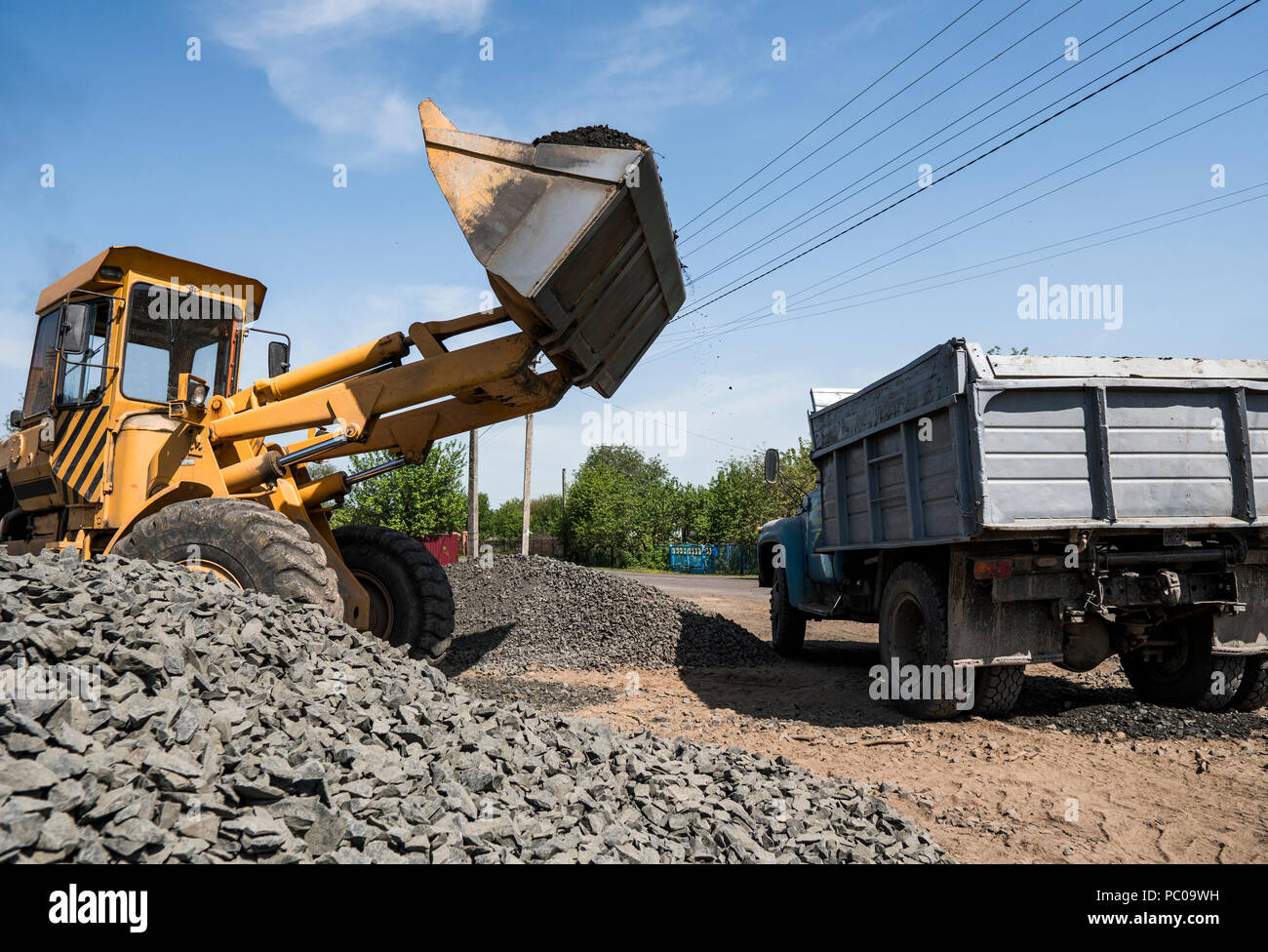 Yellow loader delivering stone gravel into truck during road ...