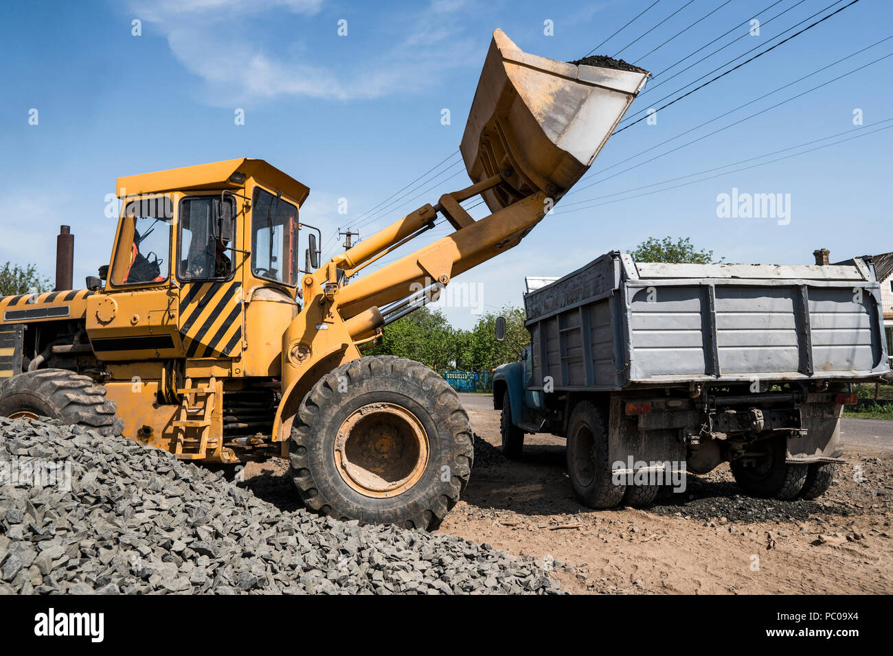 Yellow loader delivering stone gravel into truck during road ...