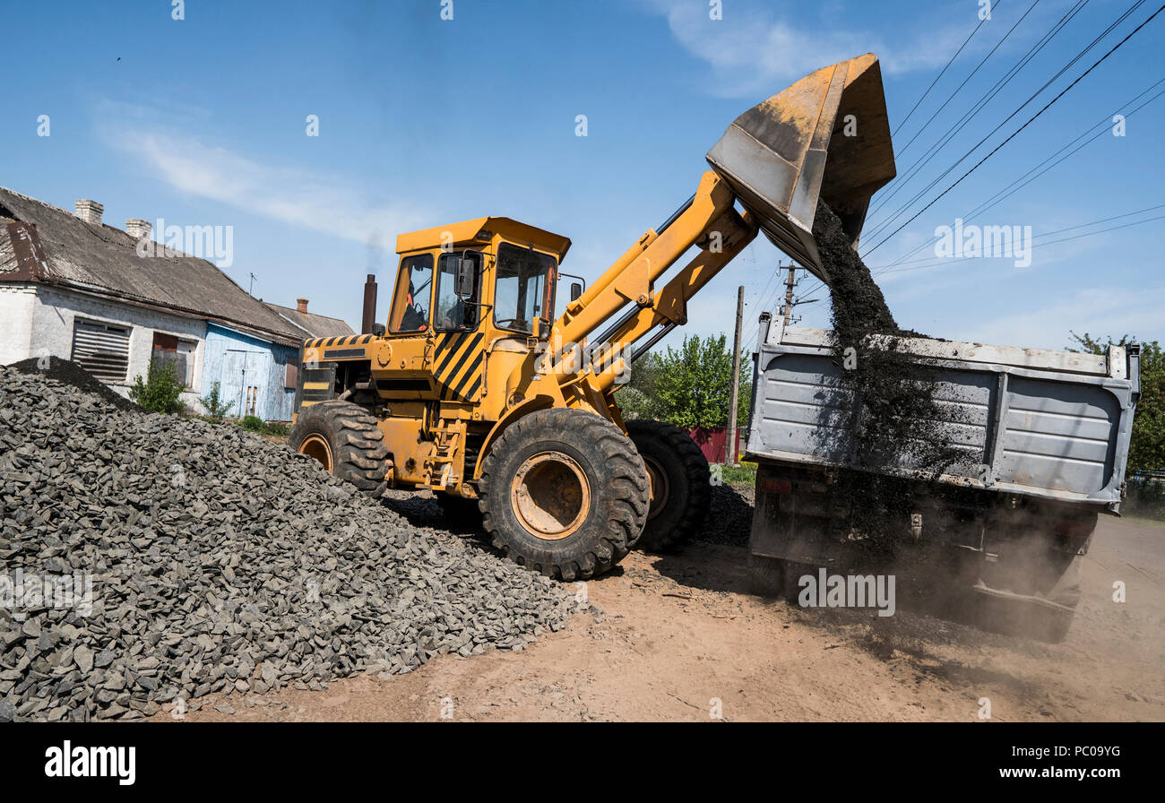 Yellow loader delivering stone gravel into truck during road ...