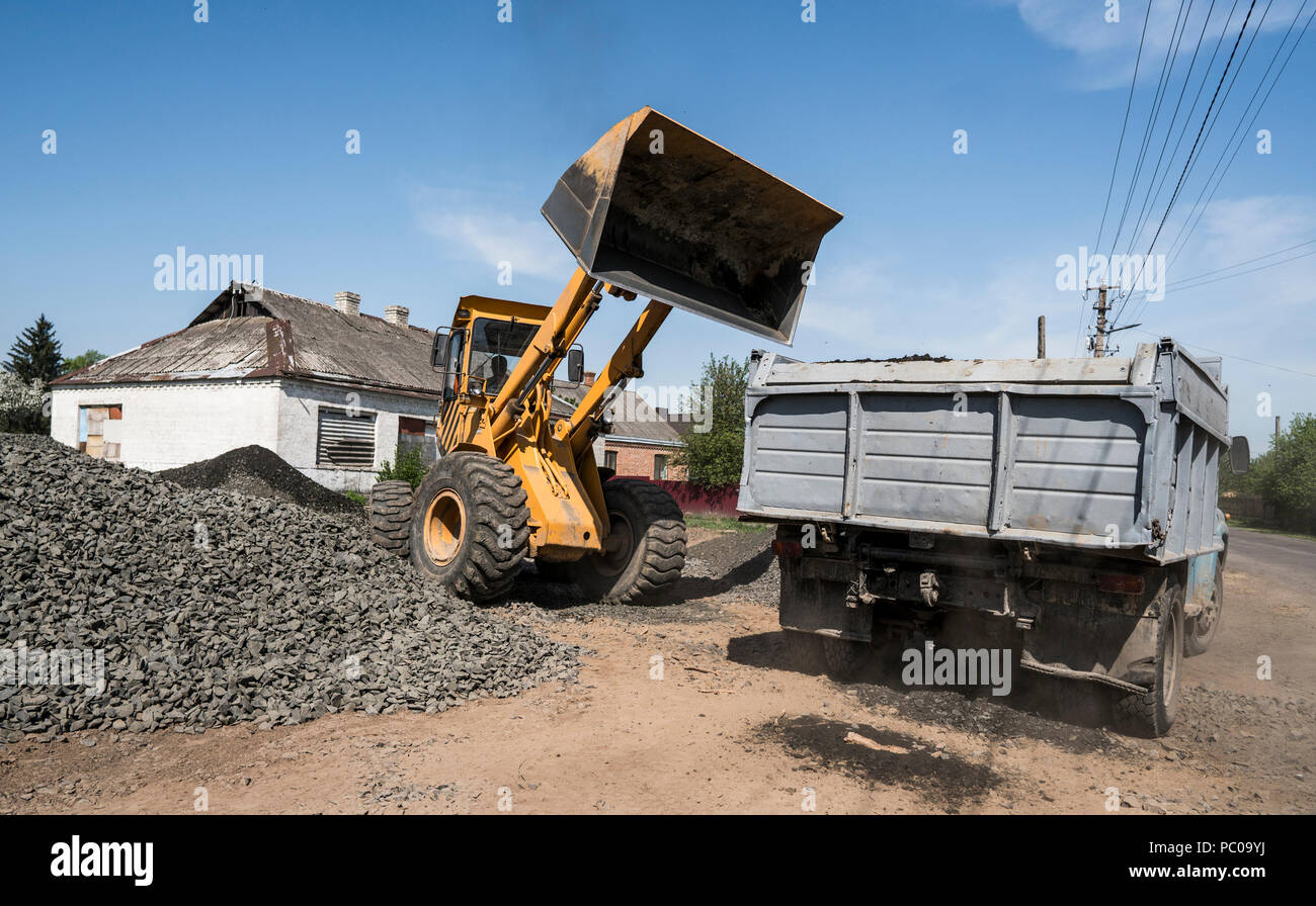 Yellow loader delivering stone gravel into truck during road ...