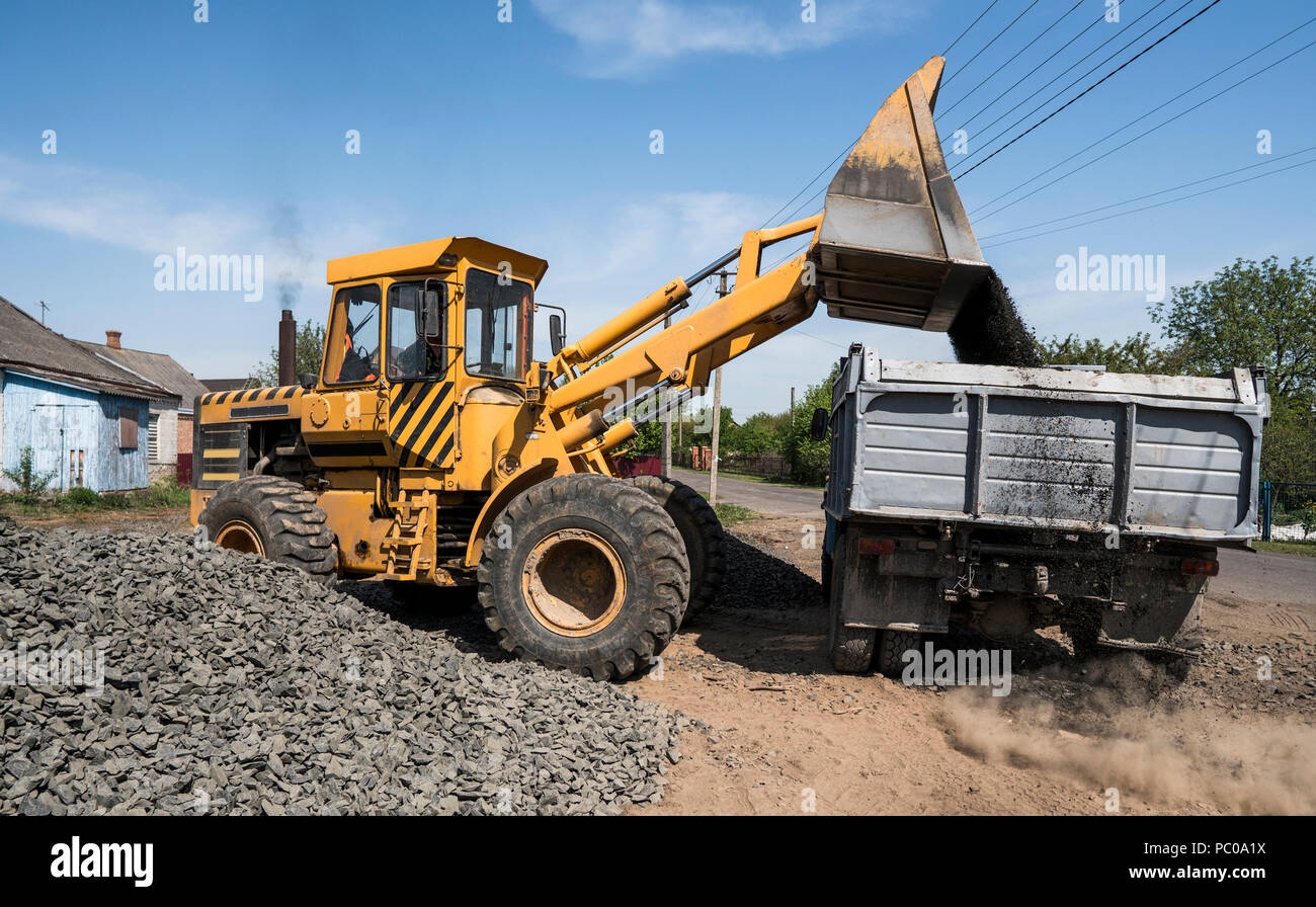 Yellow loader delivering stone gravel into truck during road ...