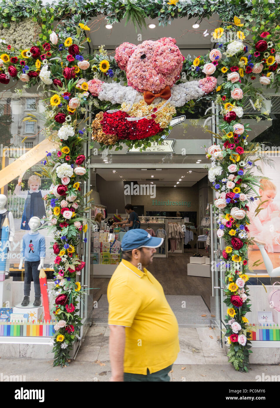 A rotun man walking in front of a floral entrance surrounding Trotters ...