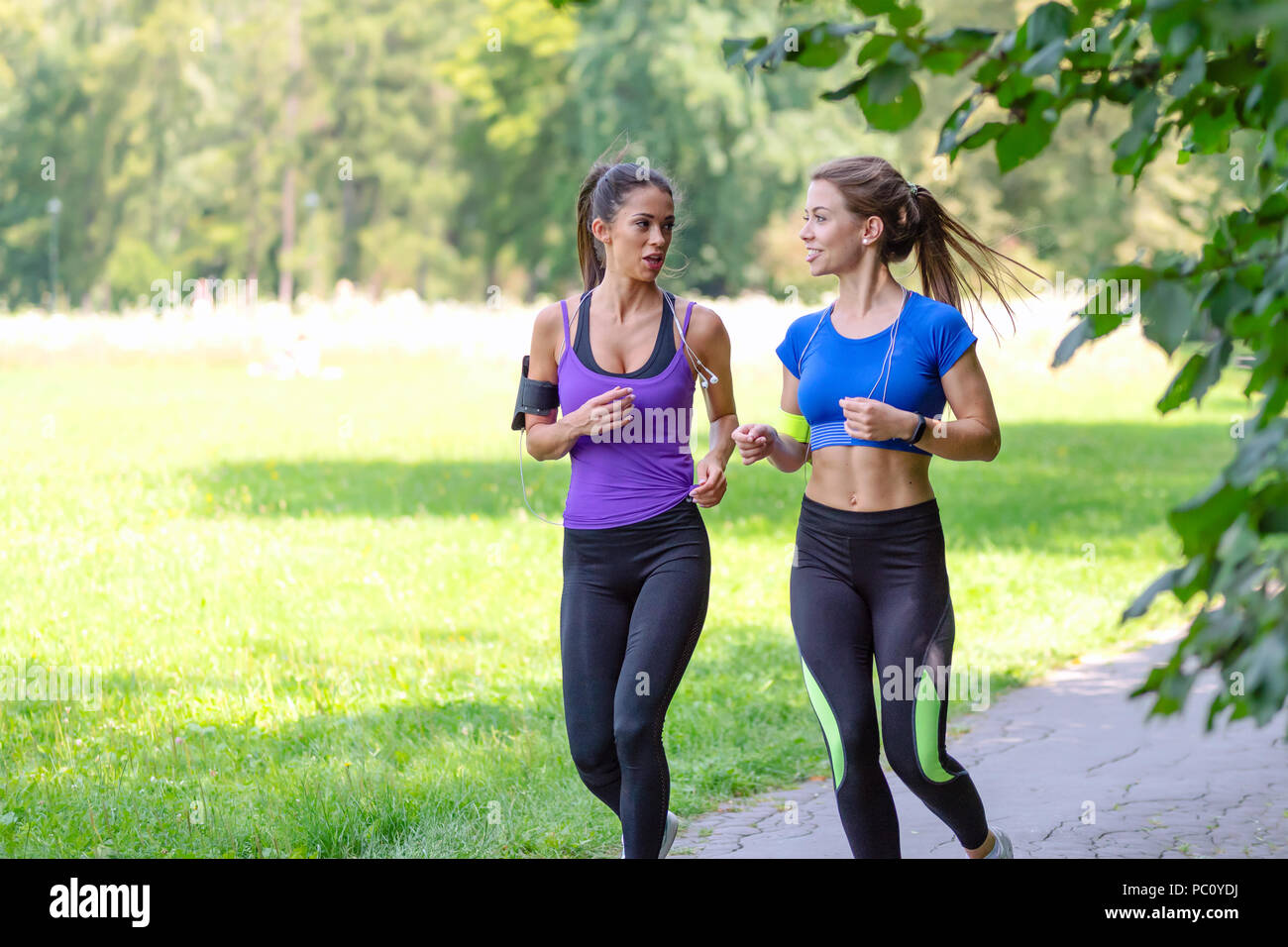 Two beautiful and attractive fitness girls are jogging in the park on a ...