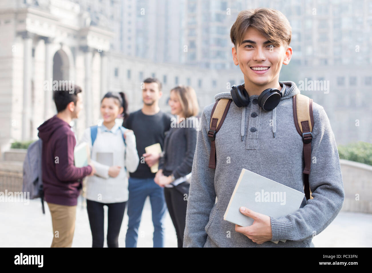Cheerful male abroad student on campus with his friends in background ...