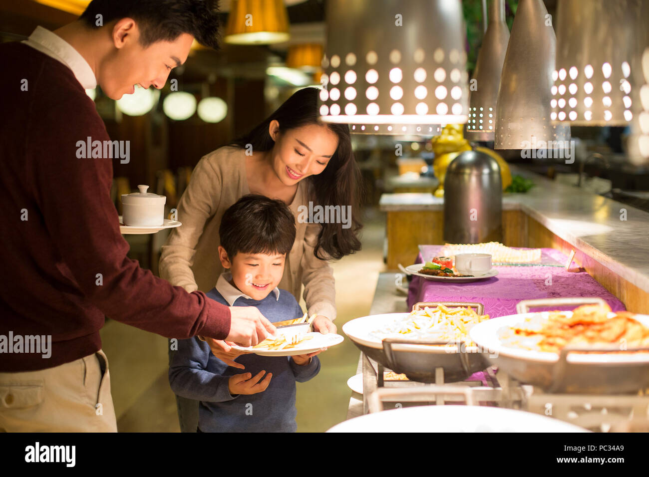 Cheerful young Chinese family taking food from buffet table Stock Photo ...