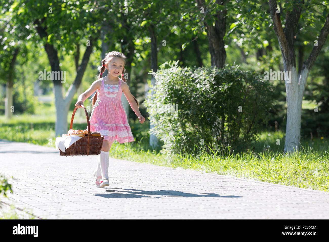 A little girl runs along the street in the city with bread and baking ...