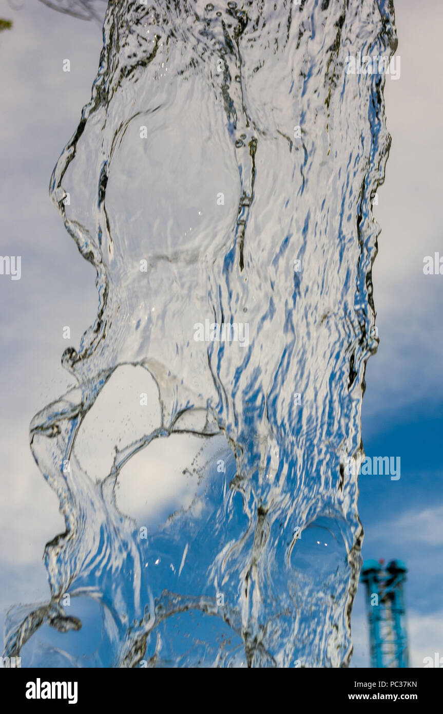 transparent falling water vertical flows against a blue sky and green ...